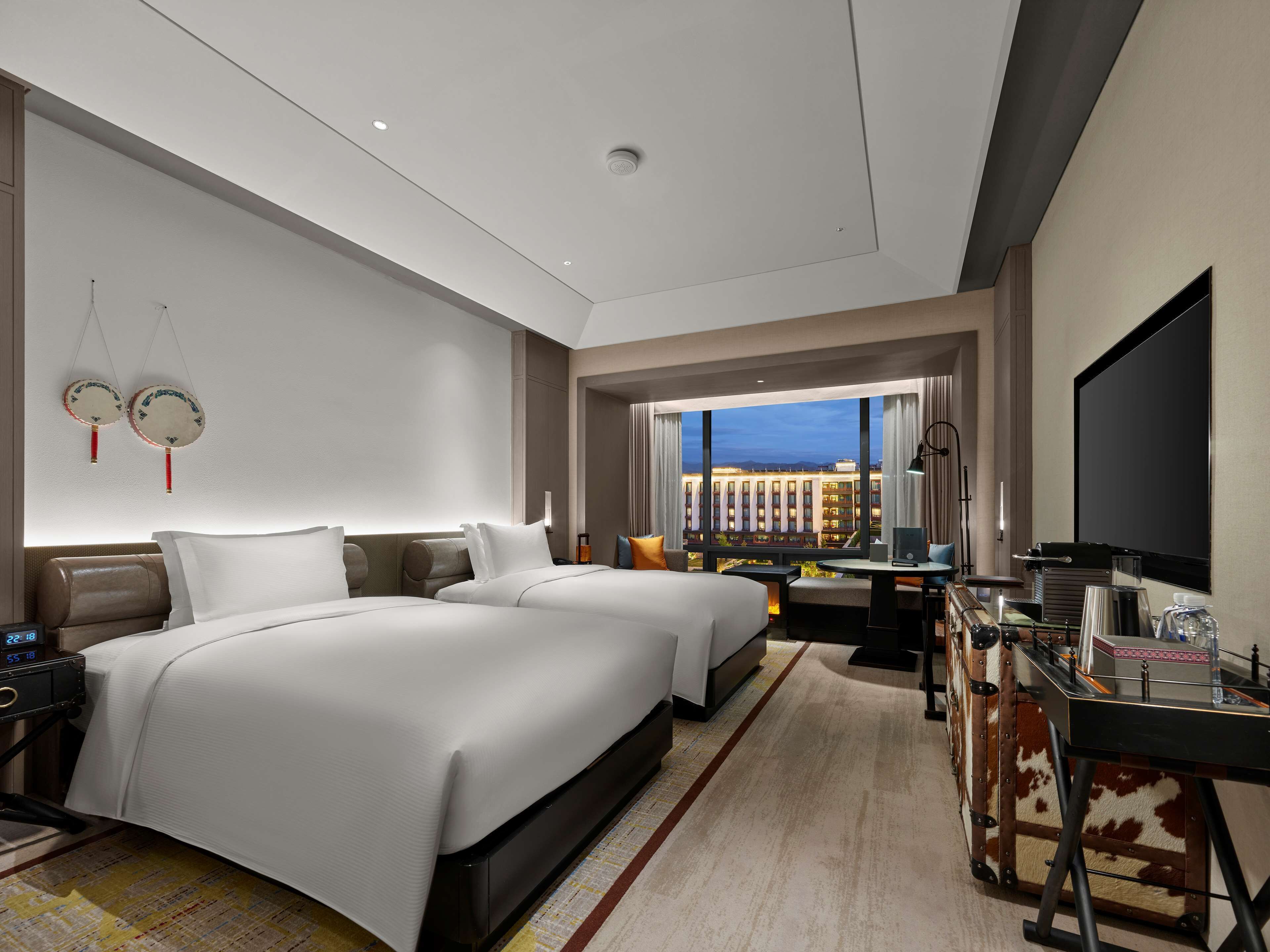 Quarto de hotel com duas camas, uma escrivaninha, televisão e vista para a cidade.