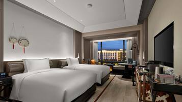 Quarto de hotel com duas camas, uma escrivaninha, televisão e vista para a cidade.