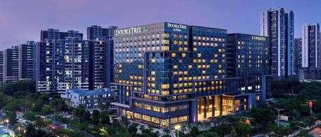 Um hotel moderno com uma placa chamativa "DOUBLETREE by Hilton", rodeado por edifícios altos e uma rua movimentada com tráfego visível.