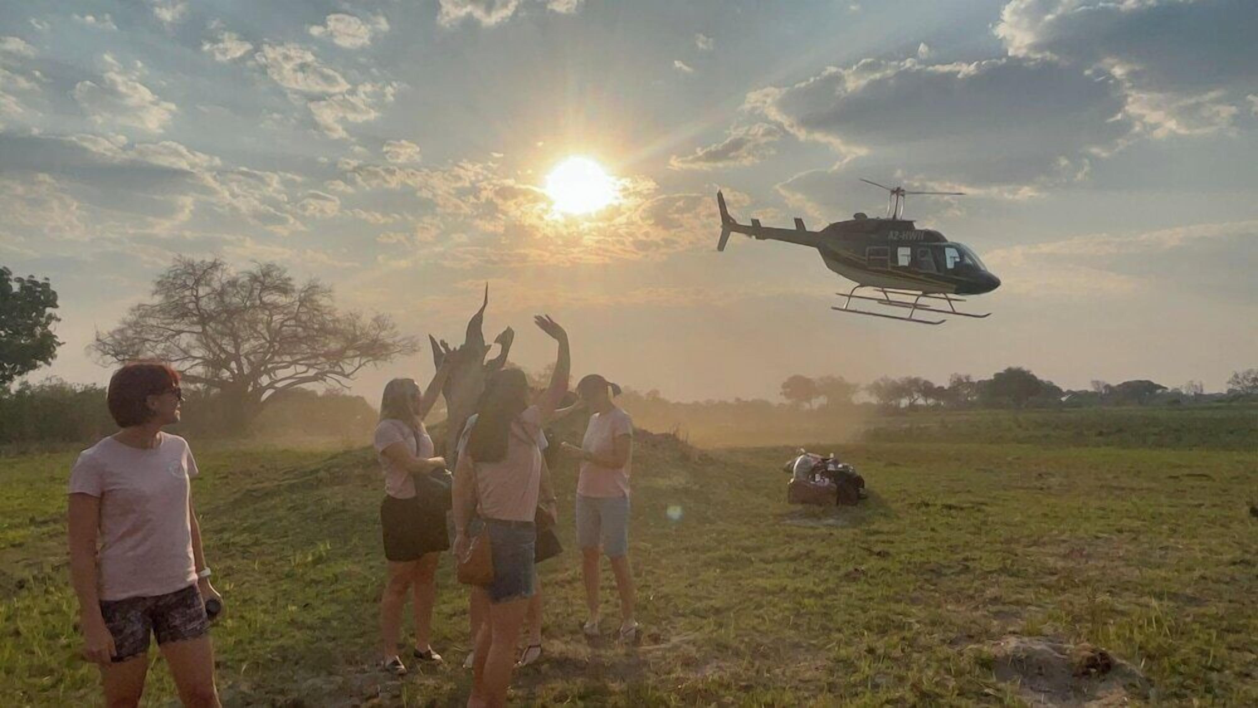 Um helicóptero sobrevoando um campo gramado com pessoas abaixo.