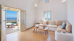 Uma sala de estar espaçosa com uma janela grande, um sofá, uma mesa de centro e vista para o mar.