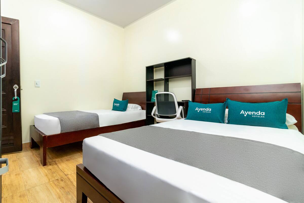 Quarto de hotel com duas camas de solteiro, cabeceira de madeira, escrivaninha e uma cadeira.