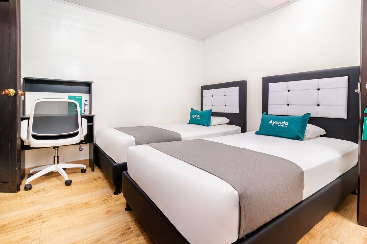 Quarto de hotel com duas camas, uma mesa e uma cadeira.