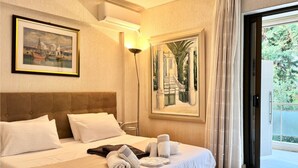 Quarto de hotel com cama, almofadas, toalhas, um quadro, uma luminária e vista para árvores através de uma janela.