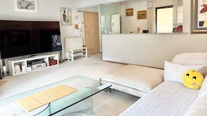 Uma sala de estar moderna com uma mesa de centro de vidro, um sofá, uma televisão e um banquinho.