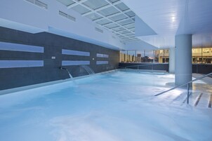Piscina interior com design moderno, apresentando uma parede escura com painéis retangulares e teto de vidro.