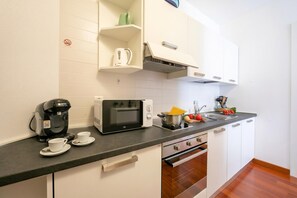 Uma cozinha compacta com cafeteira, micro-ondas e uma panela sobre o balcão.