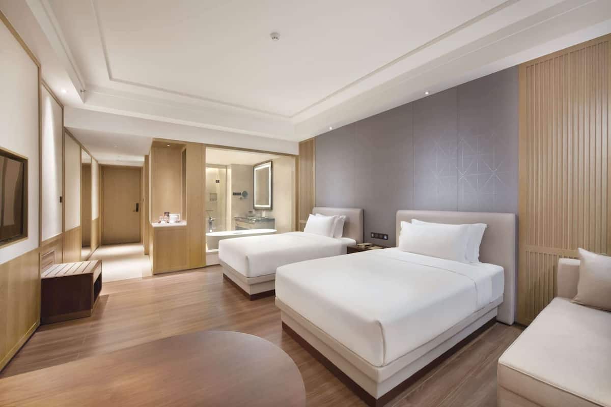 Quarto de hotel com duas camas, área de estar, banheiro e televisão.