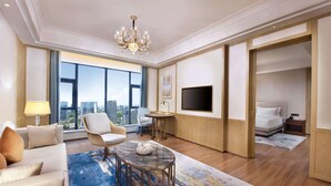 Quarto de hotel moderno com uma grande janela, um candelabro, um sofá, uma mesa de centro, uma TV e uma cama.