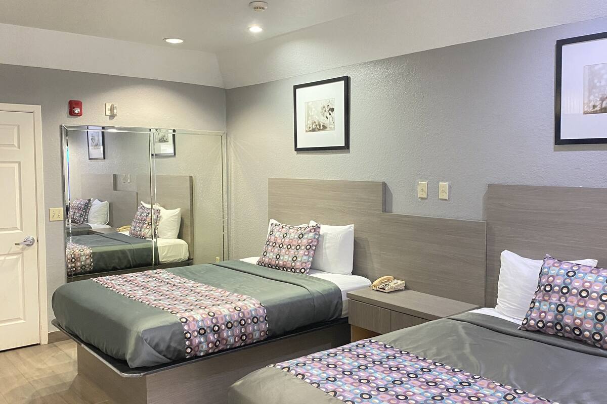 Quarto de hotel com duas camas, uma mesinha de cabeceira com telefone, um quadro na parede e uma porta com espelho.