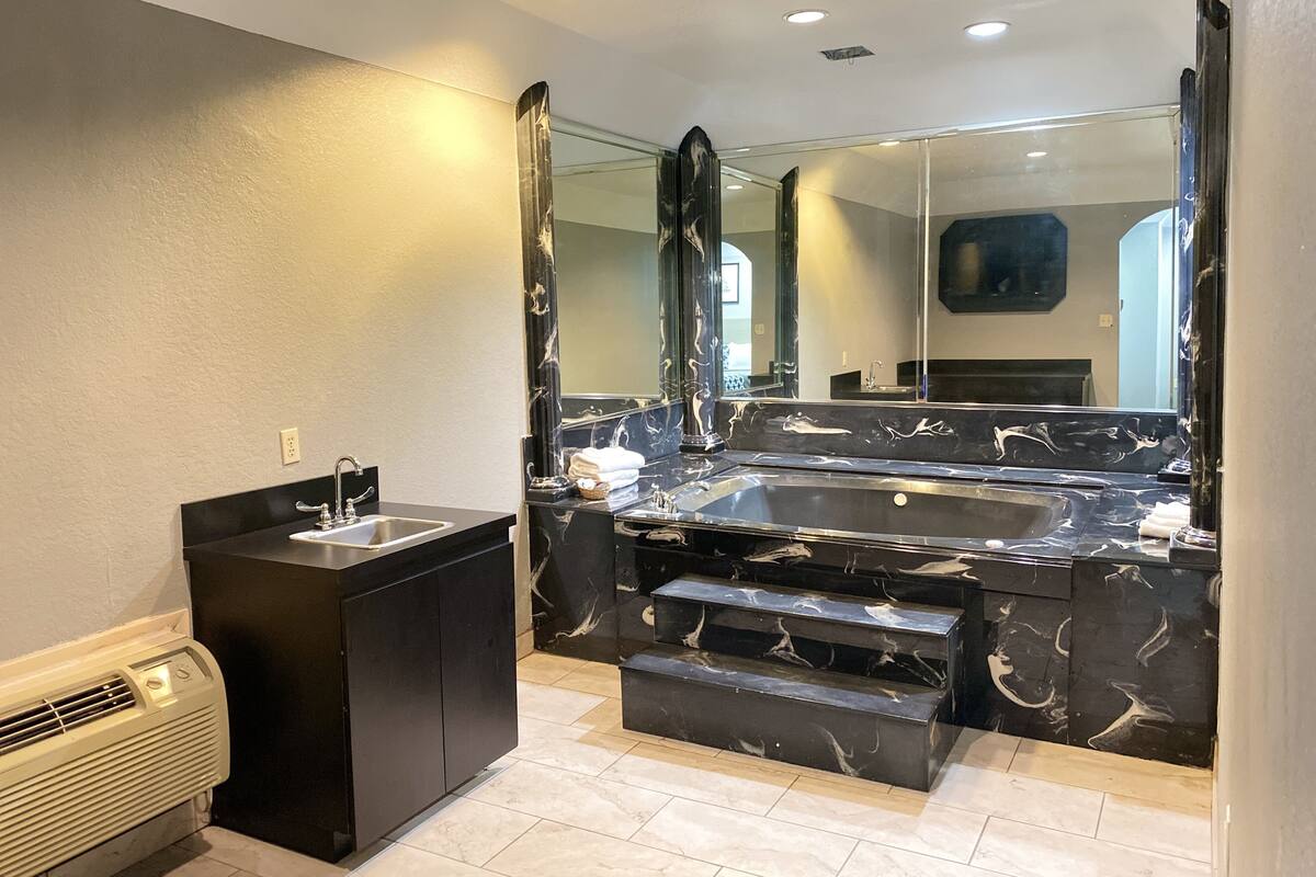 Casa de banho moderna com toucador de mármore preto, um espelho grande, uma banheira e aquecedor embutido.