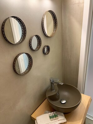Um banheiro com vários espelhos fixados na parede, uma pia com uma única torneira e um armário de vaidade de madeira.
