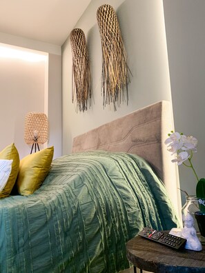 Uma cama bem arrumada com roupa de cama verde, um criado-mudo de madeira com controle remoto e detalhes decorativos nas paredes.