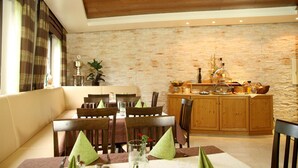 Uma área de refeições com parede de pedra ao fundo, mobiliário de madeira e um buffet.