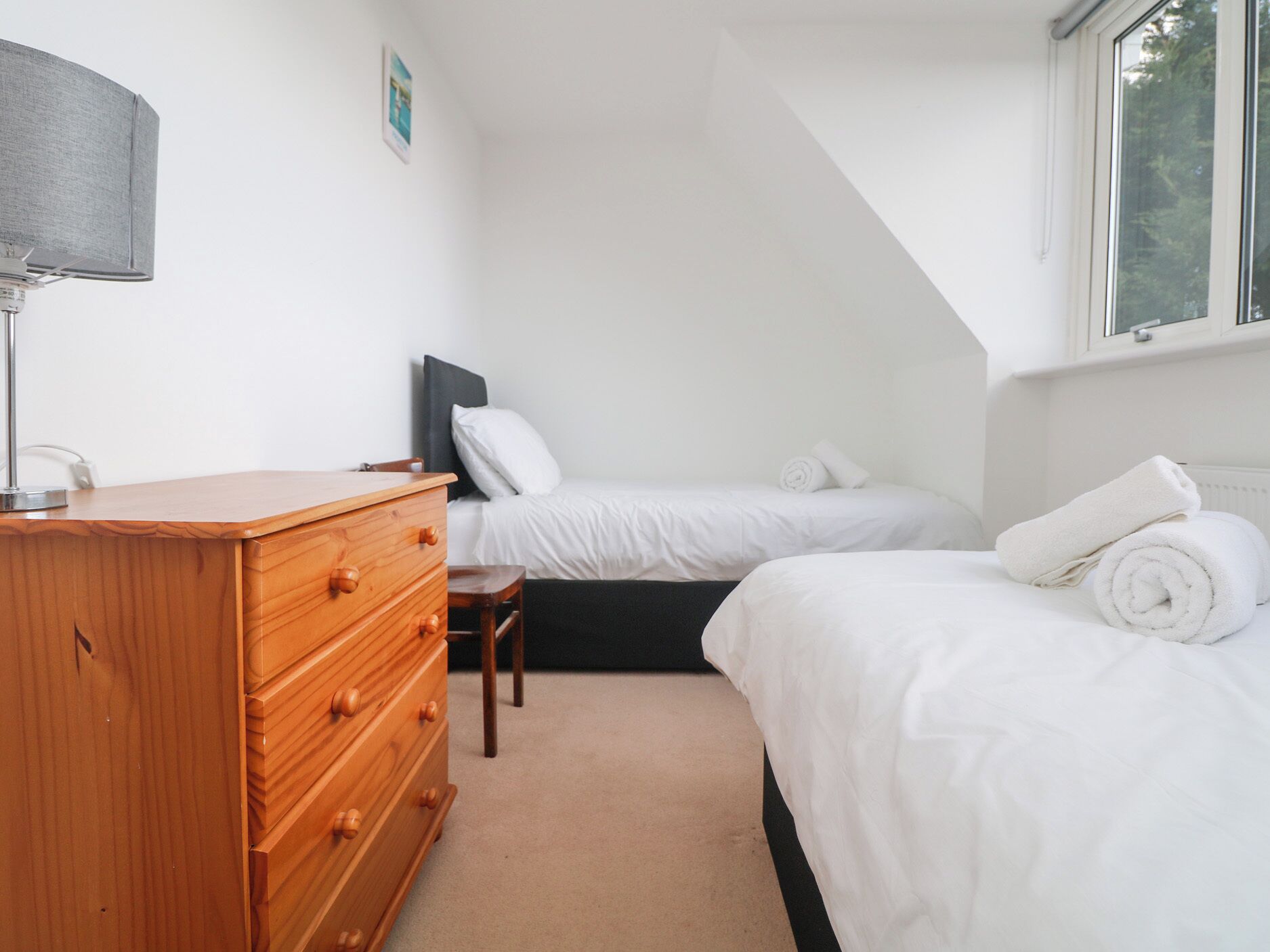 Quarto com cômoda de madeira, cama e janela.