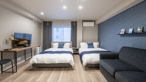 Quarto de hotel moderno com duas camas, um sofá, uma escrivaninha com televisão e uma janela grande.