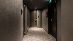 Um corredor com parede texturizada, piso coberto por carpete, porta com puxador e sinal de saída de emergência.