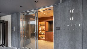 Entrada moderna de hotel com porta de vidro, balcão de recepção e interior visível com estantes de madeira e um balcão.