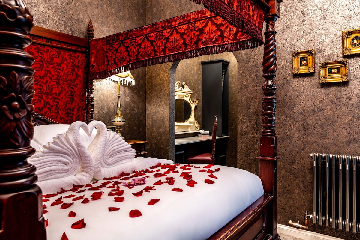 Um quarto luxuoso com uma cama grande, cabeceira elaborada e um dossel vermelho estampado.
