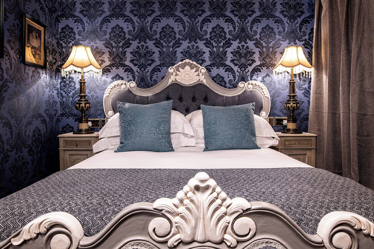 Uma cama com cabeceira estofada, duas luminárias de cabeceira e um papel de parede estampado.