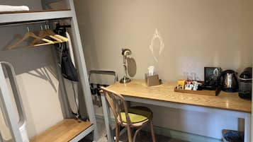 Uma cama beliche com uma escrivaninha de madeira, uma cadeira, um abajur, uma caixa de lenços, uma cafeteira e uma lixeira.