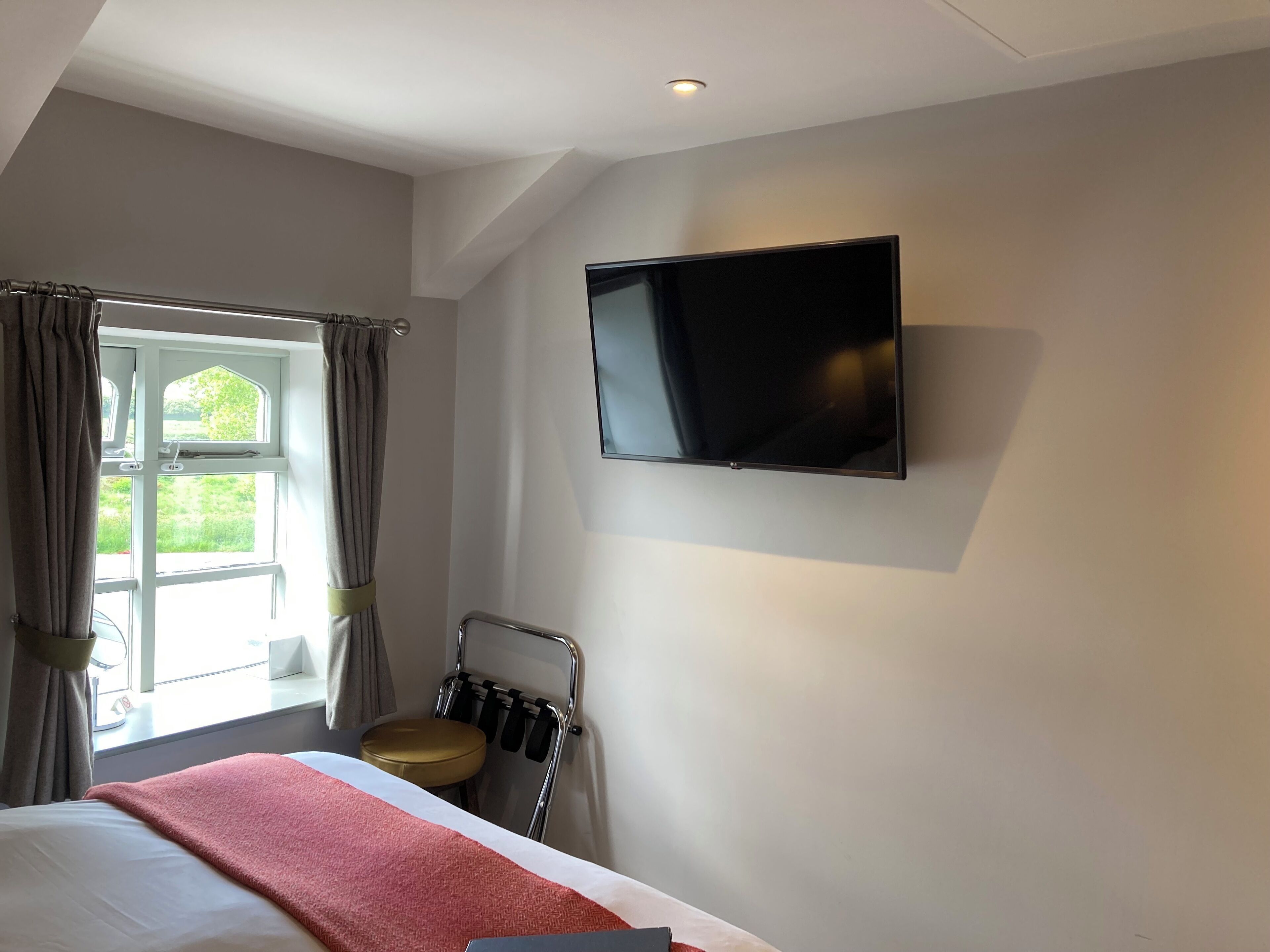 Quarto de hotel com cama, televisão na parede, janela com cortinas e radiador.