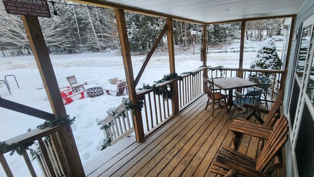 Um deck de madeira com mesa e cadeiras, rodeado por árvores cobertas de neve.
