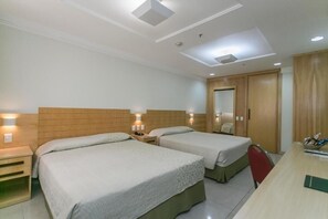 Quarto de hotel com duas camas, uma escrivaninha e um guarda-roupa.