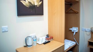 Quarto de hotel com uma prateleira de madeira, secador de cabelo, toalha, comando remoto, chaleira e garrafa de água.