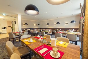 Uma sala de jantar de hotel com várias mesas, cadeiras e iluminação pendente.