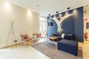 Uma sala de estar moderna com sofá, mesa de centro e cadeiras. Há uma janela grande que oferece luz natural e uma peça decorativa na parede.