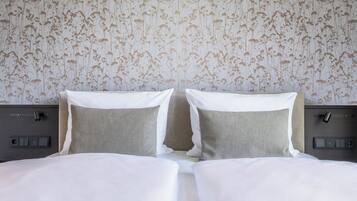 Quarto de hotel com duas camas, cada uma com roupa de cama branca e cinza.