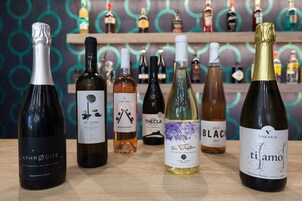 Várias garrafas de vinho sobre uma superfície de madeira, com uma parede estampada ao fundo.