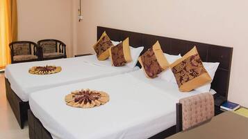 Quarto de hotel com duas camas, cada uma com um objeto decorativo e almofadas estampadas.