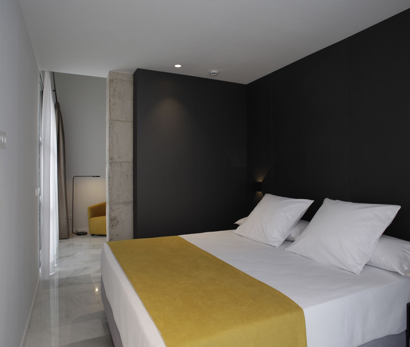 Quarto moderno com uma cama grande, um cobertor amarelo e uma parede escura de destaque.