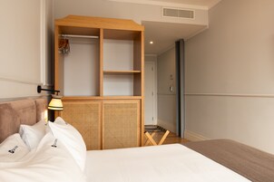Quarto de hotel com cama, guarda-roupa de madeira, abajur e porta que dá para outro espaço.