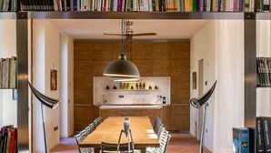 Uma zona de refeições moderna com mesa de madeira, cadeiras de metal e uma luminária pendente.