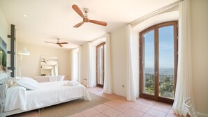 Quarto espaçoso com cama grande, duas ventoinhas no teto, banheiro com espelho e varanda com vista panorâmica.
