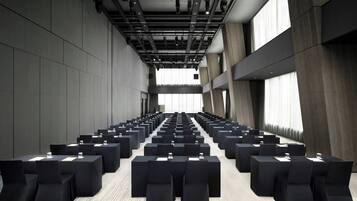 Uma sala de conferências com fileiras de mesas e cadeiras pretas, amplas janelas e um design moderno no teto.