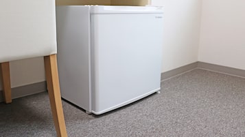 Um frigorífico branco e compacto num canto de um quarto com soalho de madeira e parede branca.
