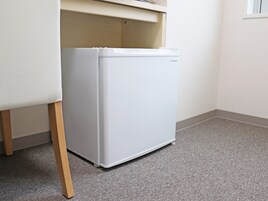 Um frigorífico branco e compacto num canto de um quarto com soalho de madeira e parede branca.