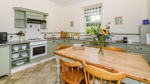 Uma cozinha com armários verdes, uma mesa de jantar de madeira e um vaso com girassóis.