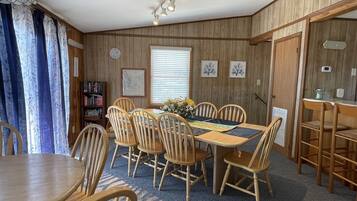 Uma sala de jantar com uma mesa e cadeiras de madeira, uma estante, um mapa e uma janela com persianas.