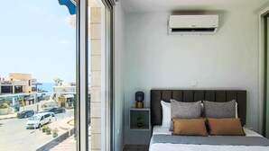 Quarto de hotel com uma janela grande, uma cama com almofadas, mesa de cabeceira com abajur e um ar condicionado.