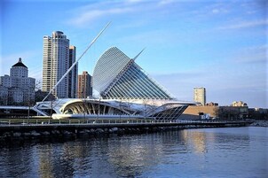 Uma estrutura arquitetônica moderna com design único, localizada à beira de um corpo d'água, rodeada por edifícios urbanos.