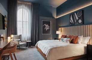 Quarto de hotel moderno com uma cama grande, uma escrivaninha, uma cadeira e uma televisão.