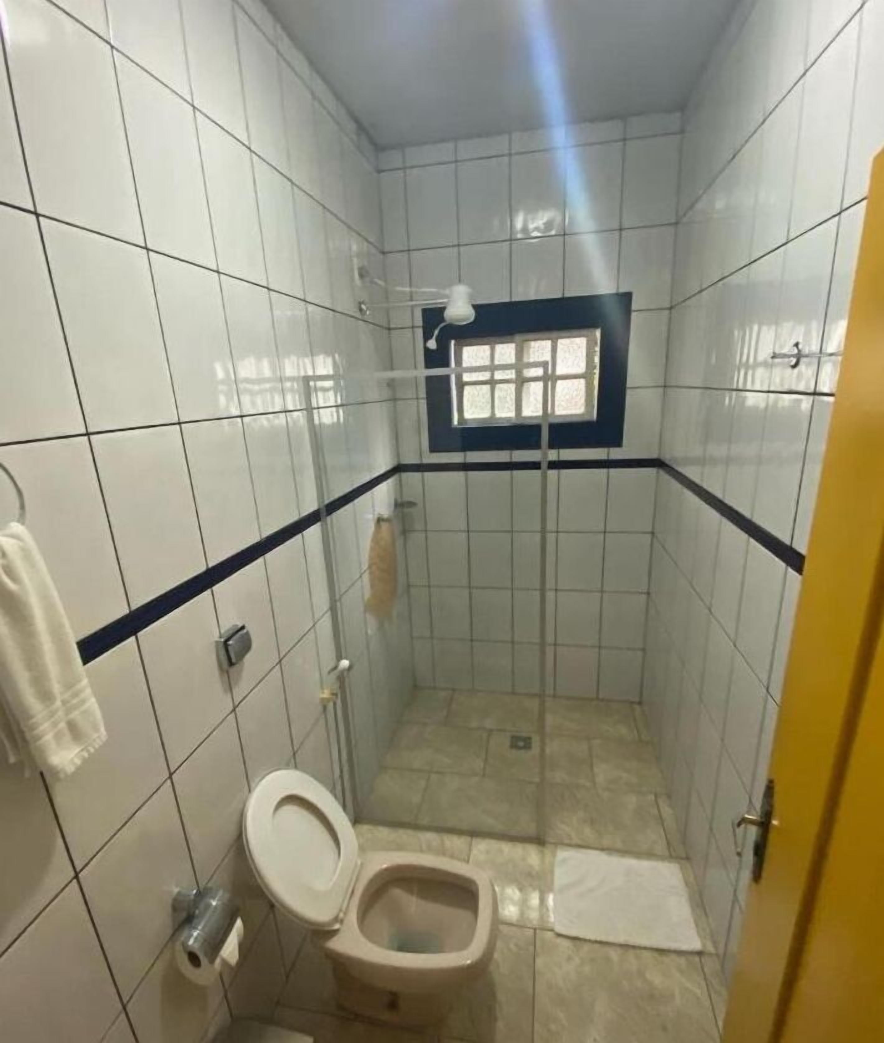 Um banheiro pequeno com azulejos, vaso sanitário, box de chuveiro e janela.