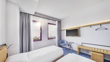 Quarto de hotel com duas camas, uma escrivaninha, uma cadeira, uma televisão e uma janela com cortinas.