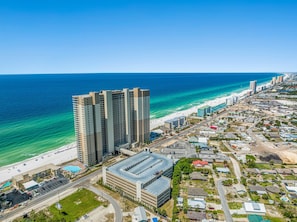Um hotel costeiro com vários edifícios altos, uma praia e um parque de estacionamento.