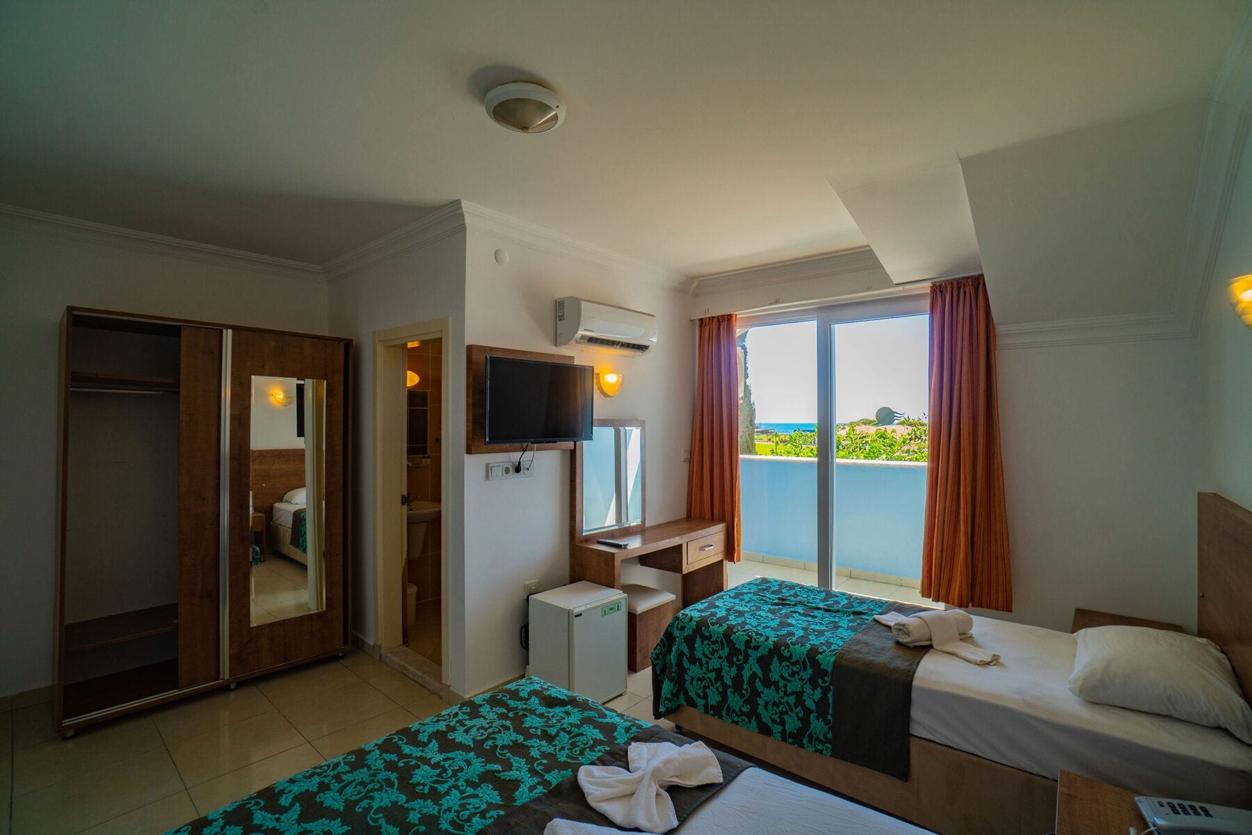 Quarto de hotel com duas camas, uma escrivaninha, televisão e varanda com vista.